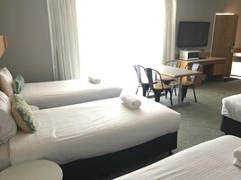 Quarto de hotel com duas camas, uma escrivaninha, uma cadeira e uma televisão.