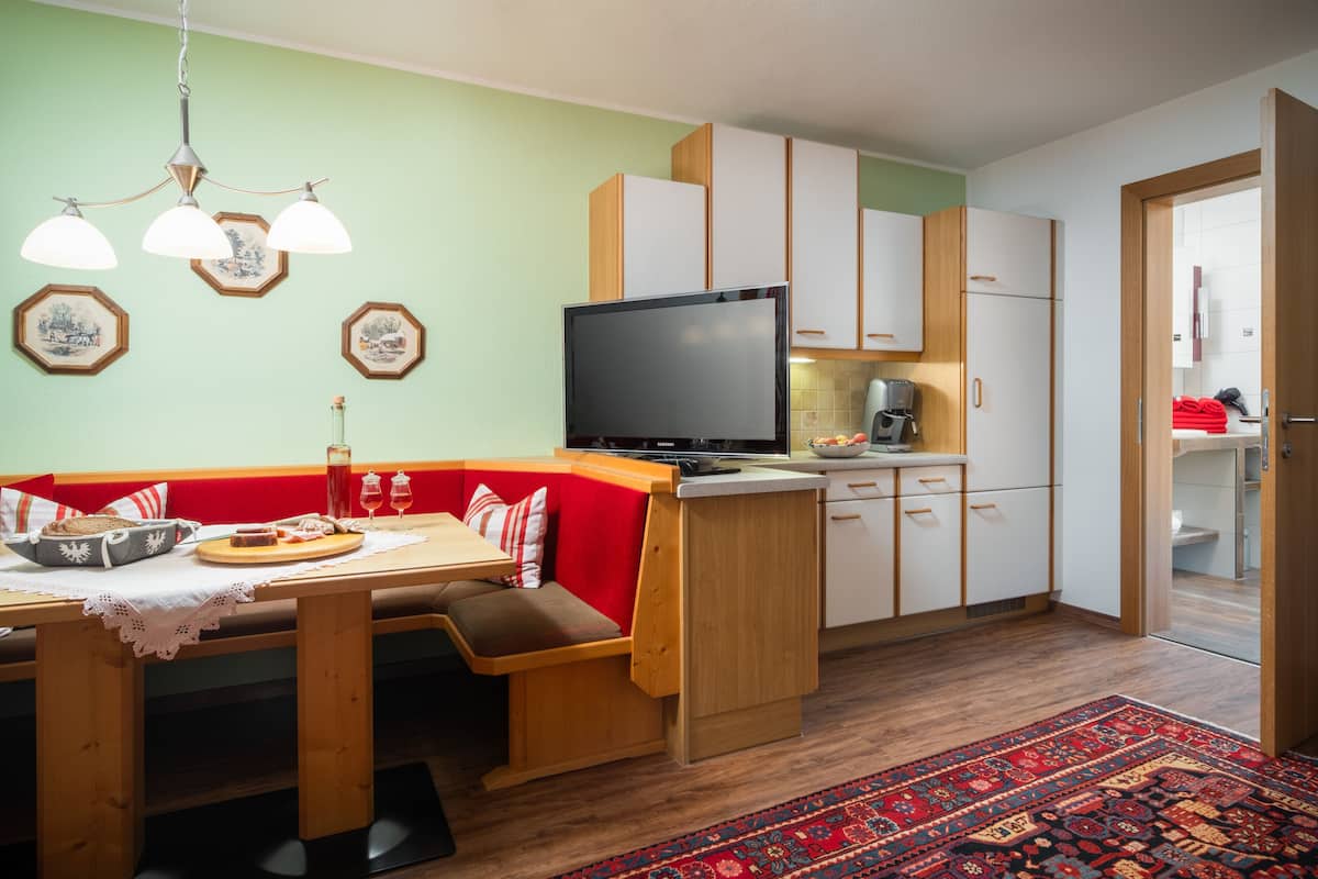 Uma cozinha compacta com área de refeições, armários de madeira, uma TV embutida e um banco vermelho.