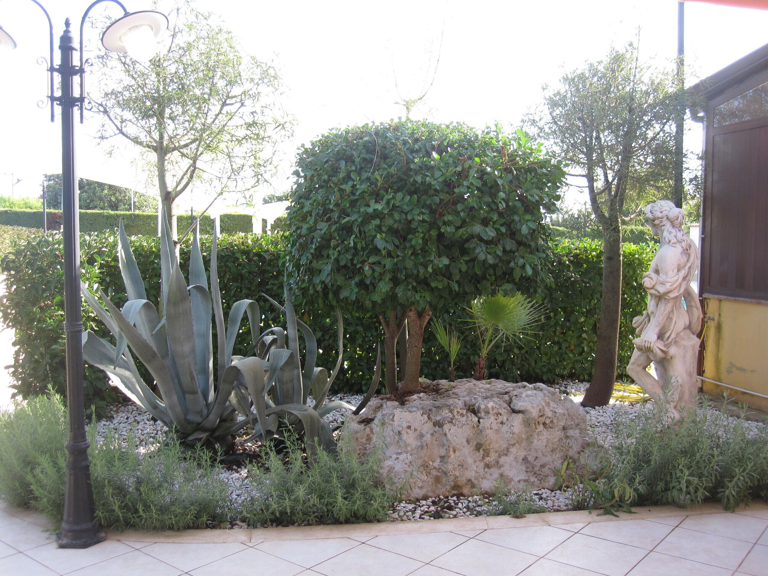 Um jardim com uma estátua, um poste de luz e diversas plantas.