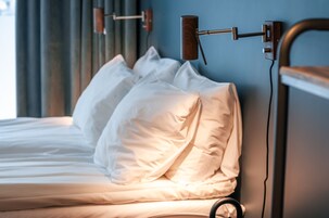 Cama bem arrumada com lençóis brancos e cabeceira de madeira.
