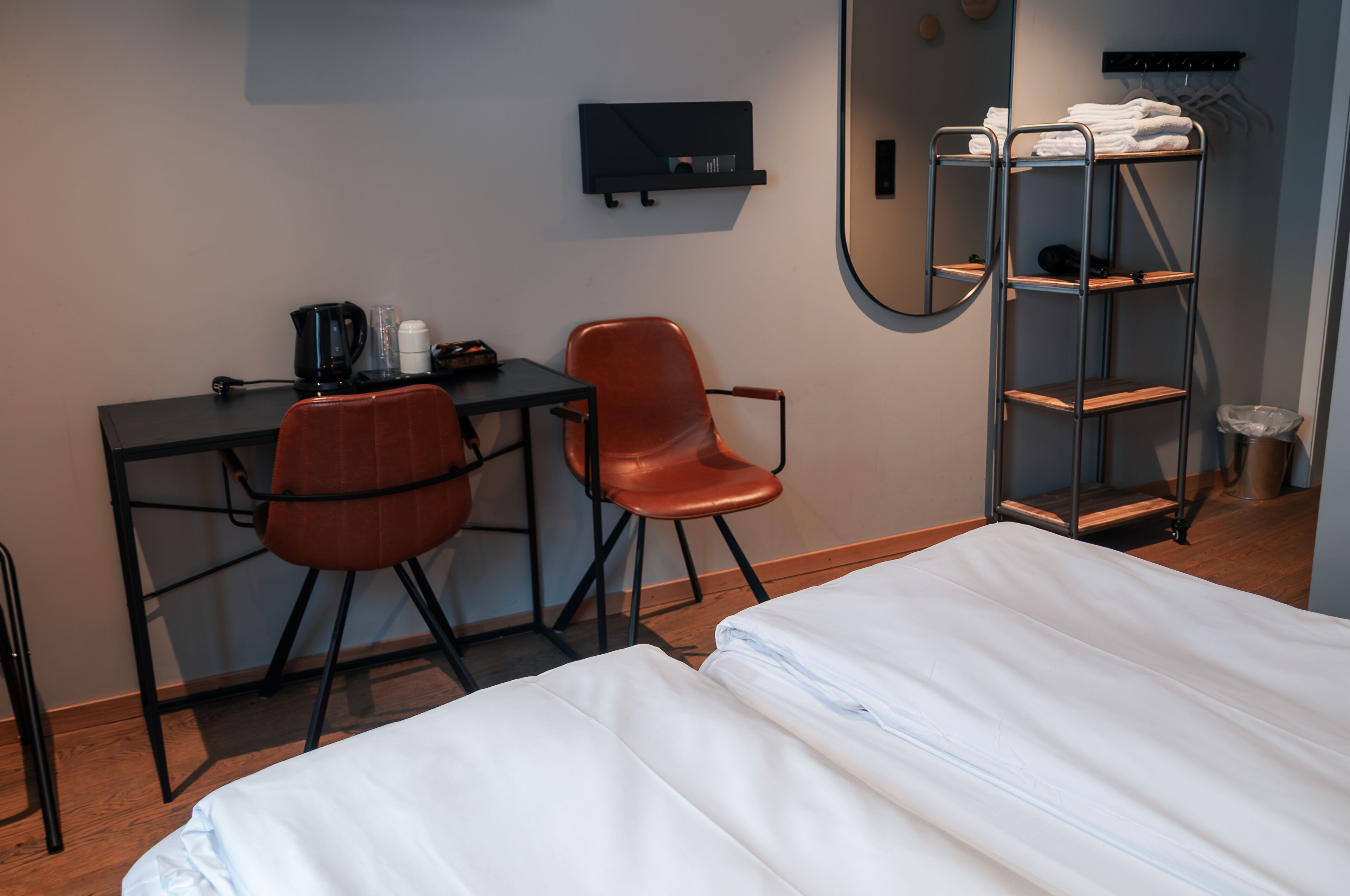 Quarto de hotel com cama, escrivaninha, cadeira, cafeteira e prateleira com toalhas.