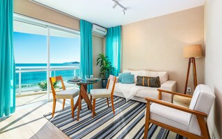Uma varanda com vista para o oceano, um espaço de refeições com cadeiras e mesa, um sofá com almofadas e um abajur.