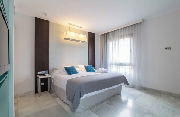 Quarto de hotel moderno com uma cama grande, uma mesinha de cabeceira, uma luminária na parede e uma janela com cortinas.