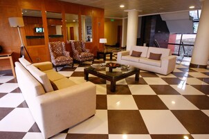Um hall com piso xadrez, um sofá, poltronas, uma mesa de centro e um abajur.