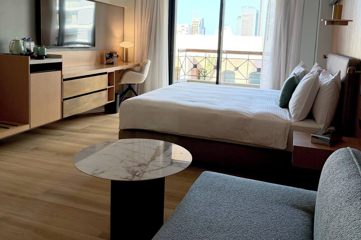 Quarto de hotel moderno com cama, escrivaninha, TV e varanda com vista para a cidade.
