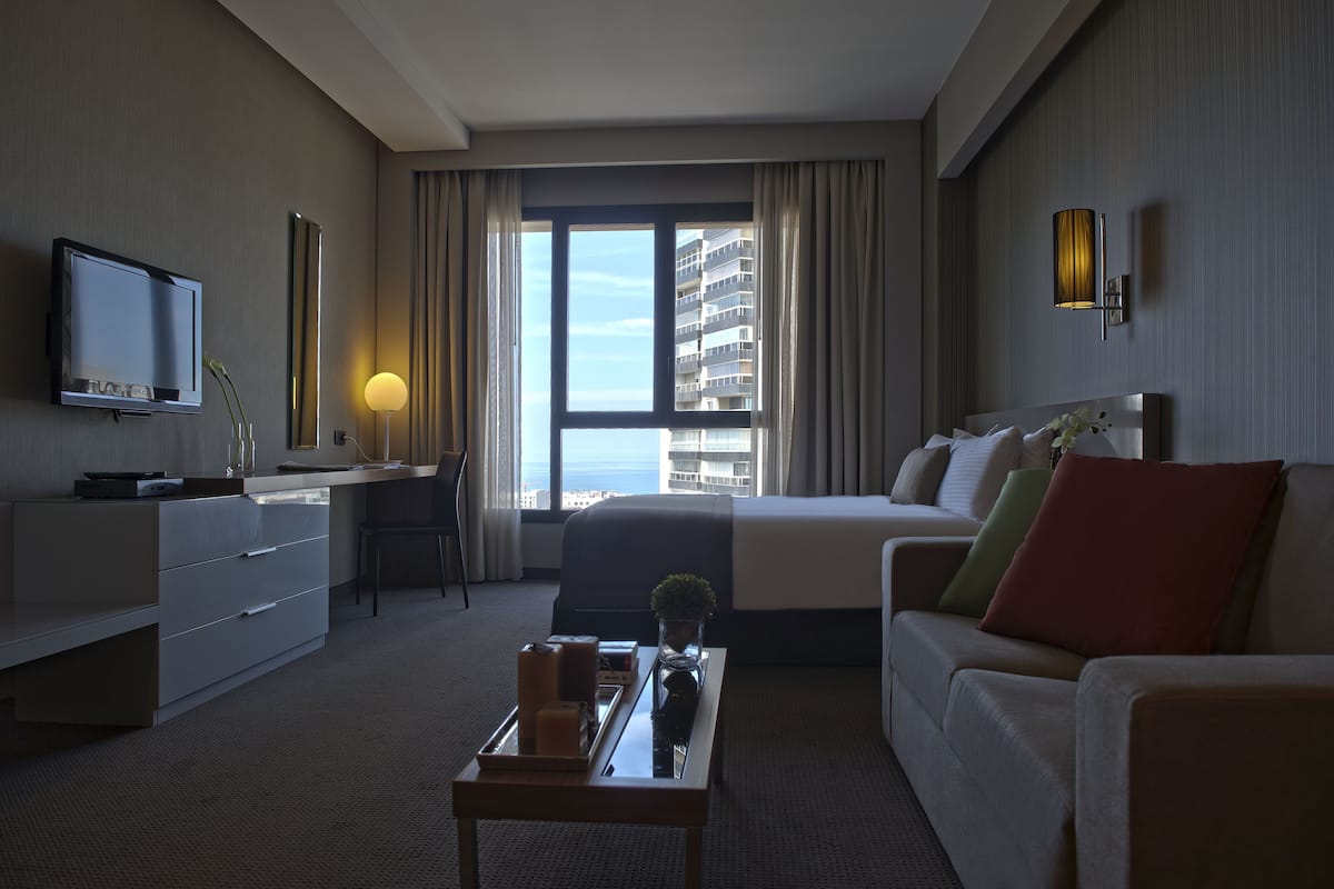 Quarto de hotel com cama, mesa de escritório com televisão, mesa de centro e vista para a cidade.