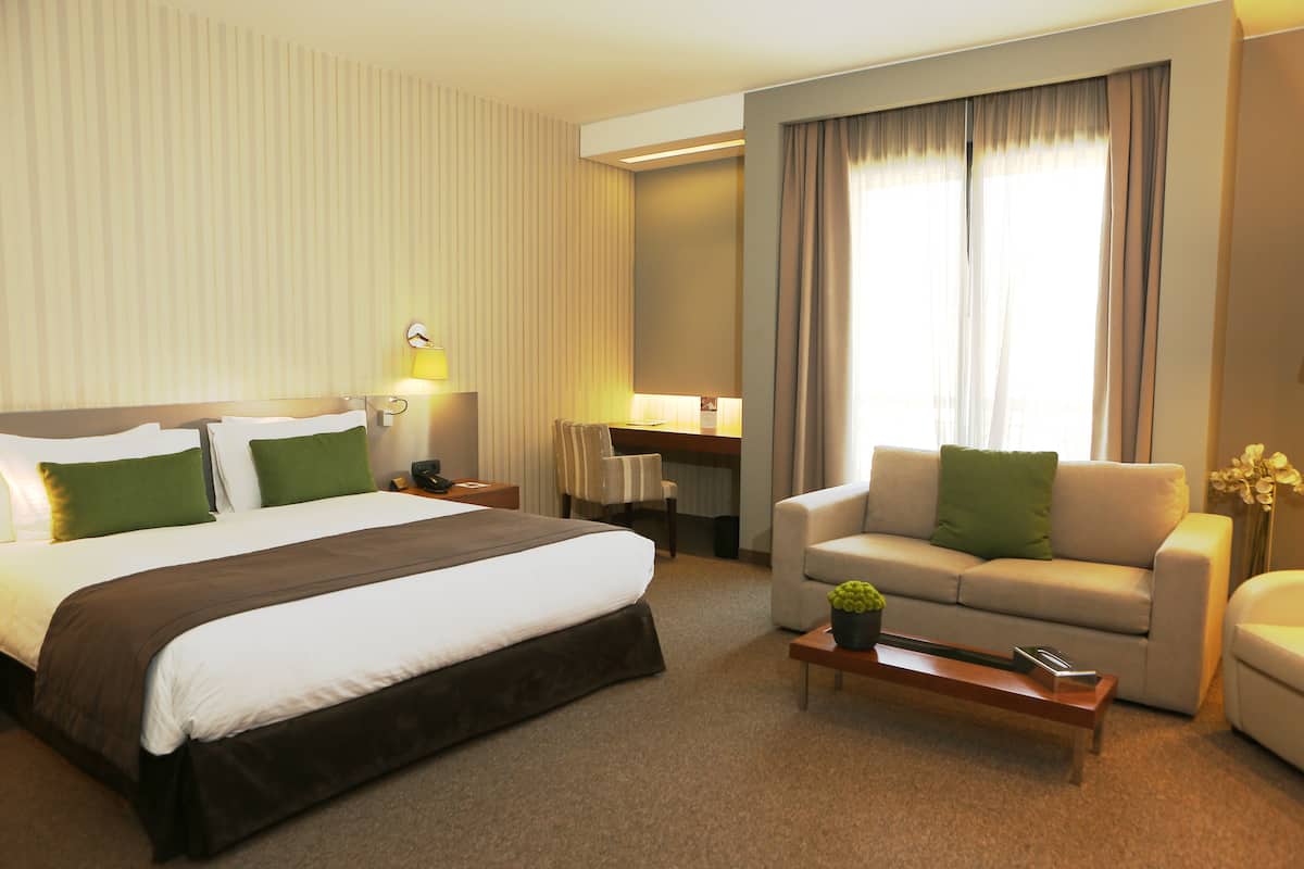 Quarto de hotel com uma cama grande, um sofá, uma escrivaninha e uma mesa de centro.