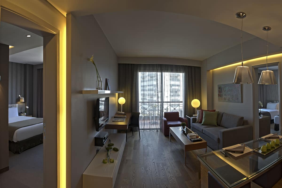 Quarto de hotel moderno com cama, escrivaninha, sofá e varanda com vista.