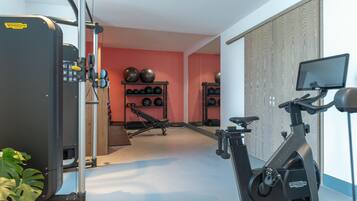 Uma academia em casa com uma bicicleta ergométrica, um banco de musculação, um suporte para agachamento e uma prateleira com bolas de exercício.