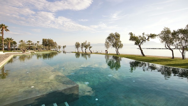 Uma piscina infinita transparente com vista para o mar e palmeiras.