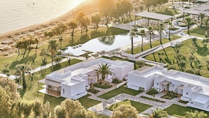 Um resort costeiro com edifícios brancos modernos, piscina e área de praia com guarda-sóis.