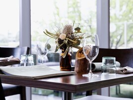 Uma mesa de jantar com um menu, um copo de água, uma taça de vinho e um vaso com flores.