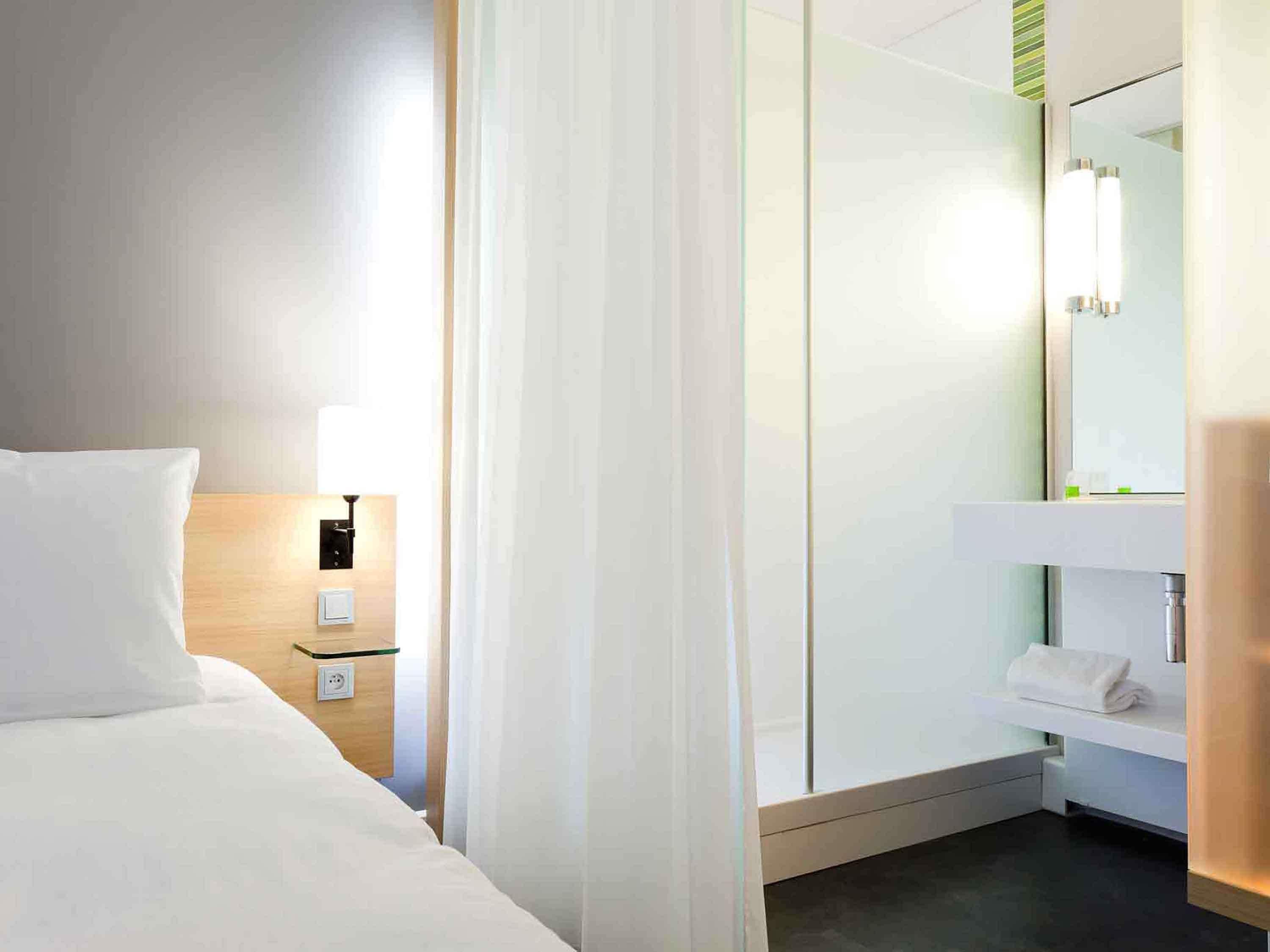 Quarto de hotel com uma cama, mesa de cabeceira, banheiro com espelho e porta-toalhas.
