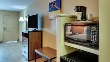 Quarto de hotel compacto com televisão, micro-ondas, uma mesinha e armário com gavetas.