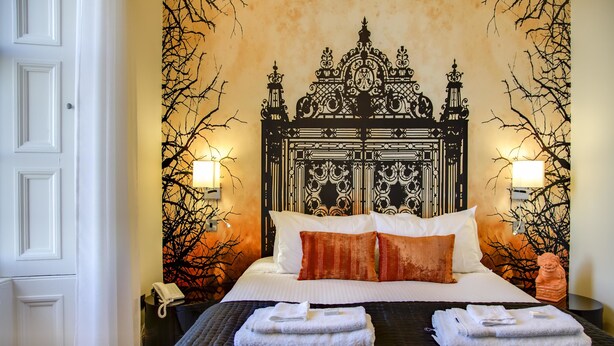 Quarto de hotel com uma cama grande, duas luminárias de cabeceira e uma cabeceira decorativa.