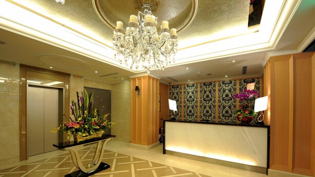 Um hall com balcão de recepção, um candelabro, um arranjo de flores e um piso estampado.