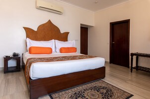 Quarto com cama de madeira, roupa de cama branca e laranja, tapete estampado e mesa de cabeceira de madeira.