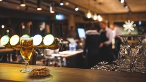 Um balcão com um copo de cerveja, um recipiente com castanhas e copos vazios.