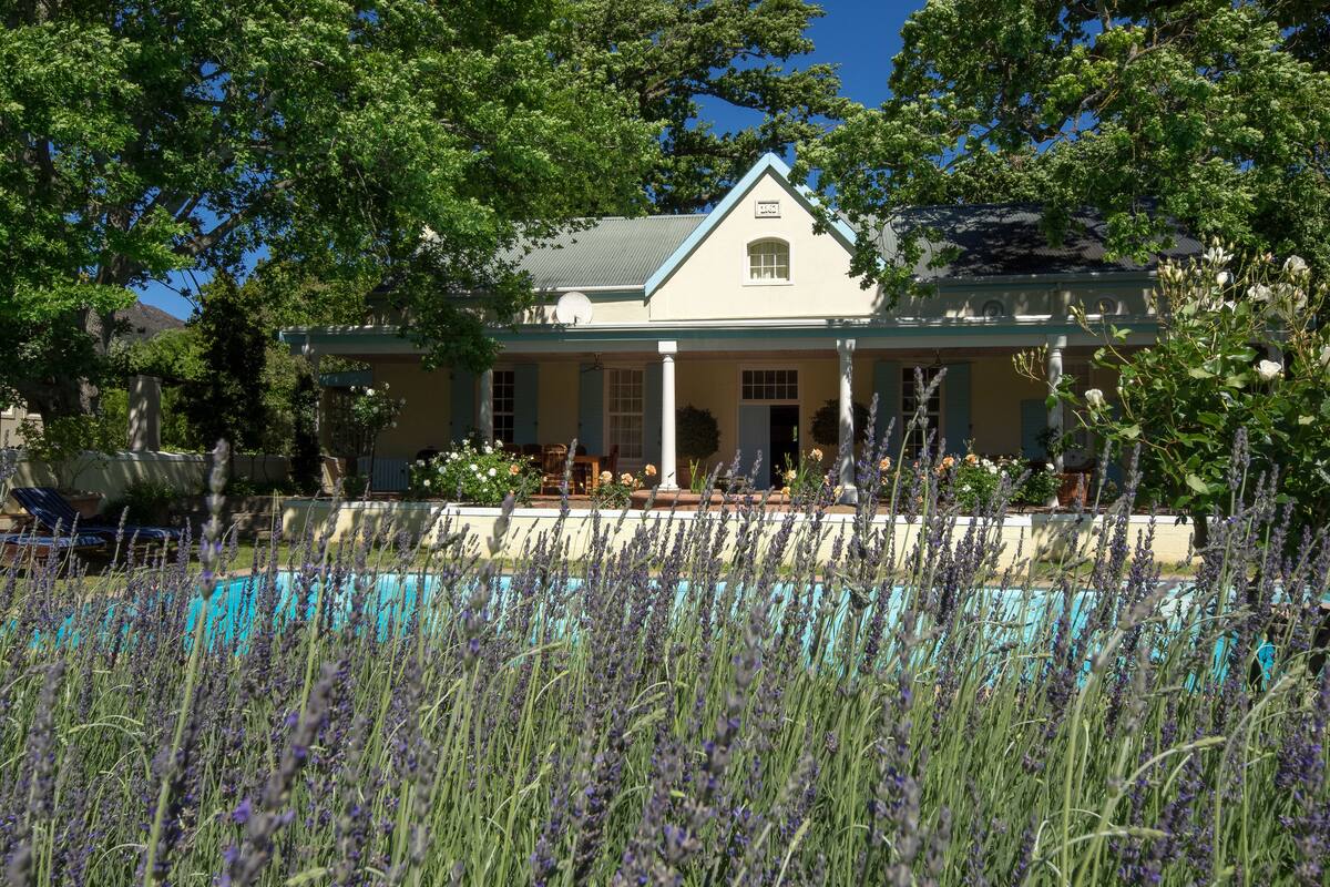 Uma casa de dois andares com varanda da frente, piscina e jardim com plantas de lavanda.