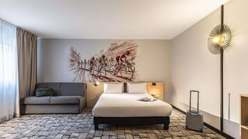 Quarto de hotel com cama, sofá, painel na parede, abajur e mala.