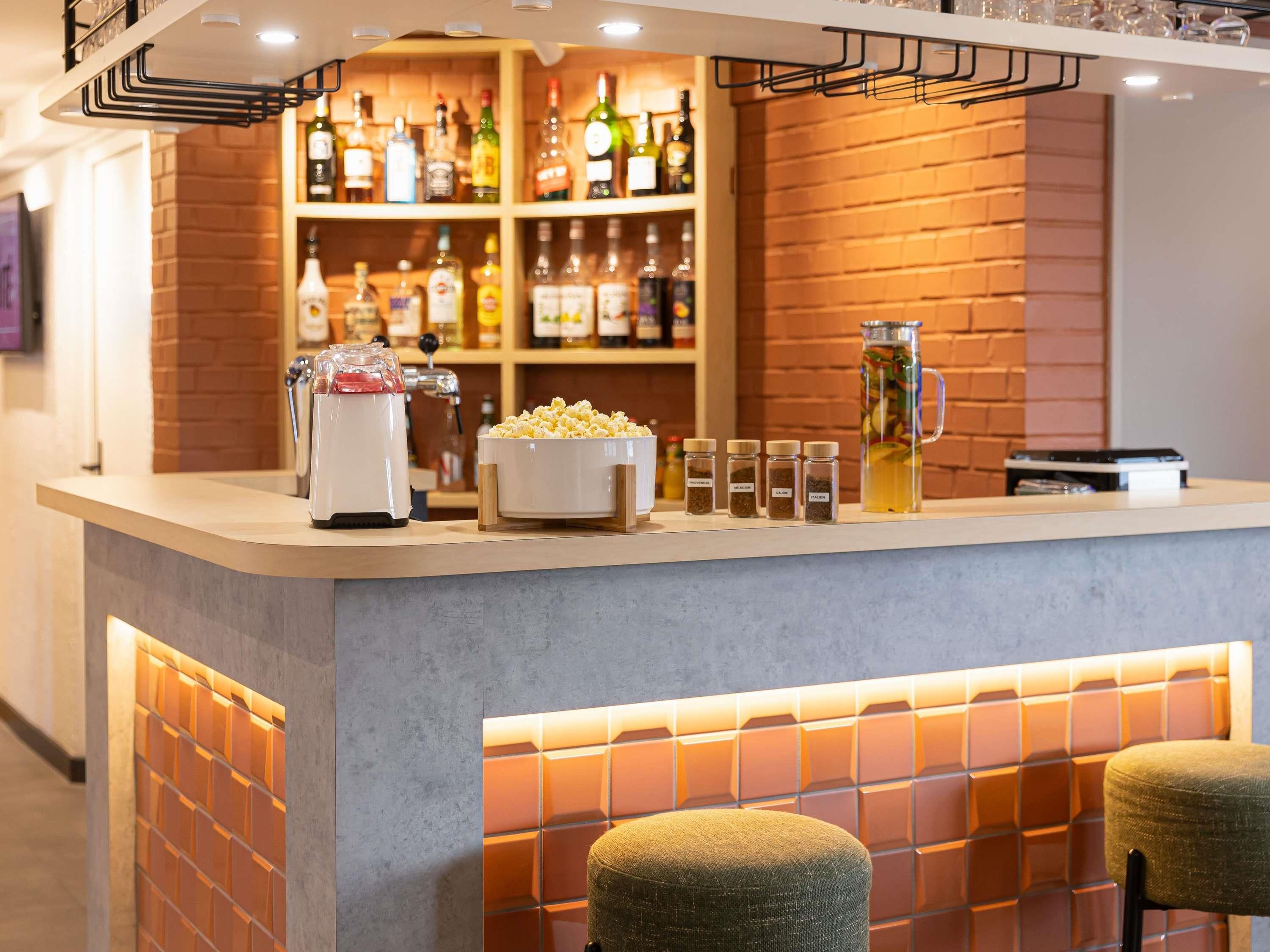 Uma área de bar com bancada, garrafas, jarra e um recipiente com pipoca.