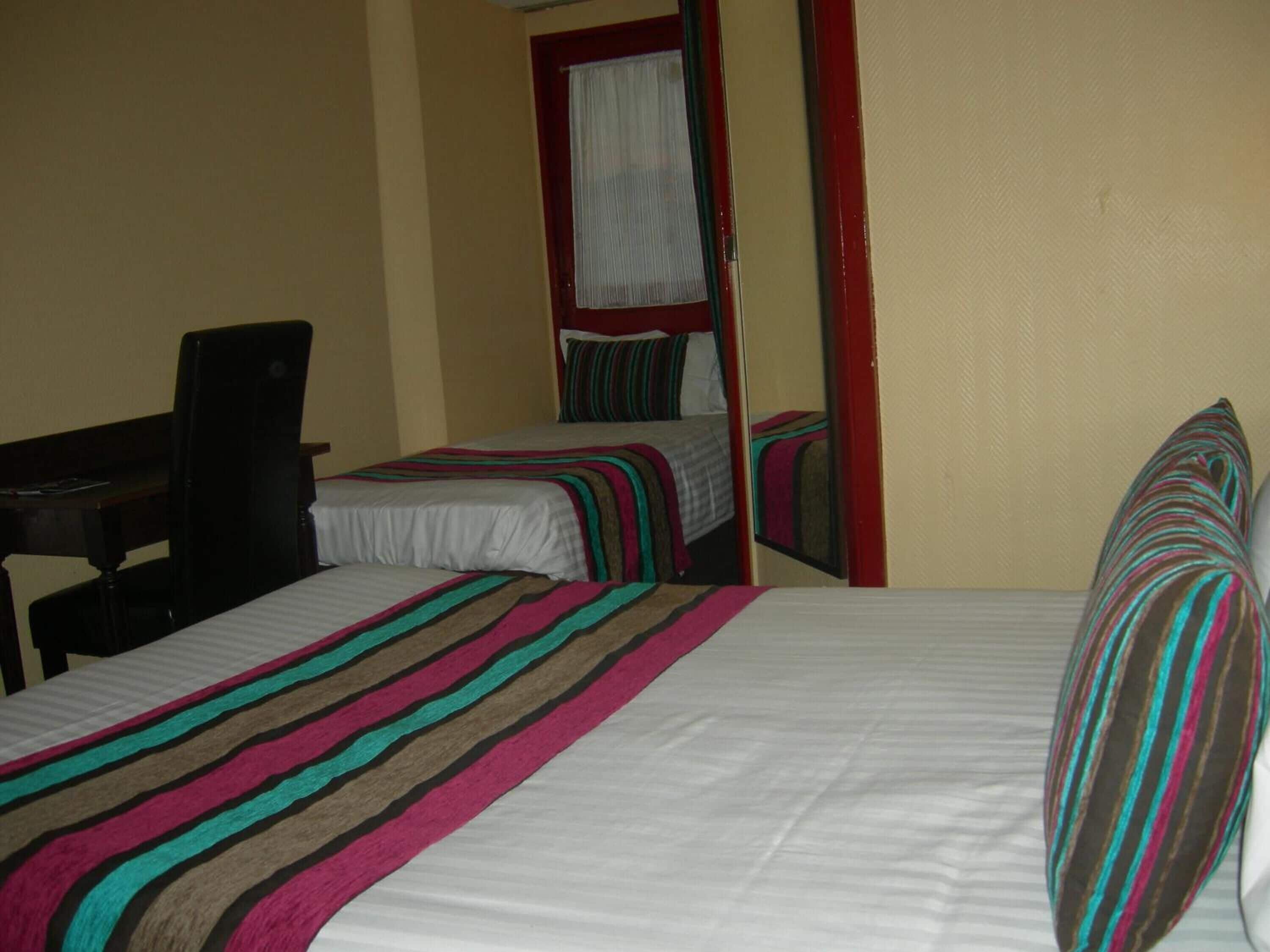 Quarto de hotel com duas camas de solteiro, uma escrivaninha e uma cadeira.