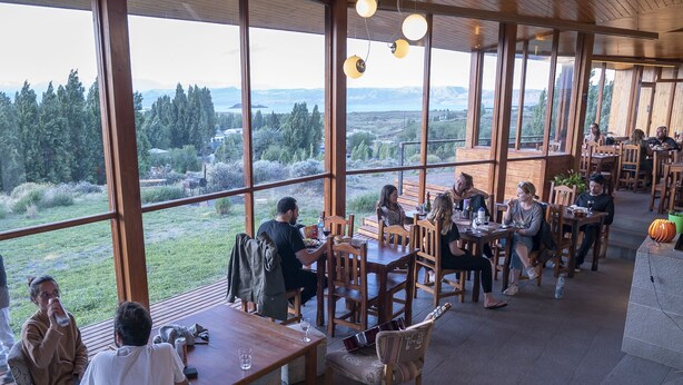 Uma sala de jantar espaçosa com grandes janelas que oferecem vista para o exterior. Mesas e cadeiras dispostas para refeições.