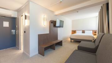 Quarto de hotel com cama, área de estar, televisão e porta.