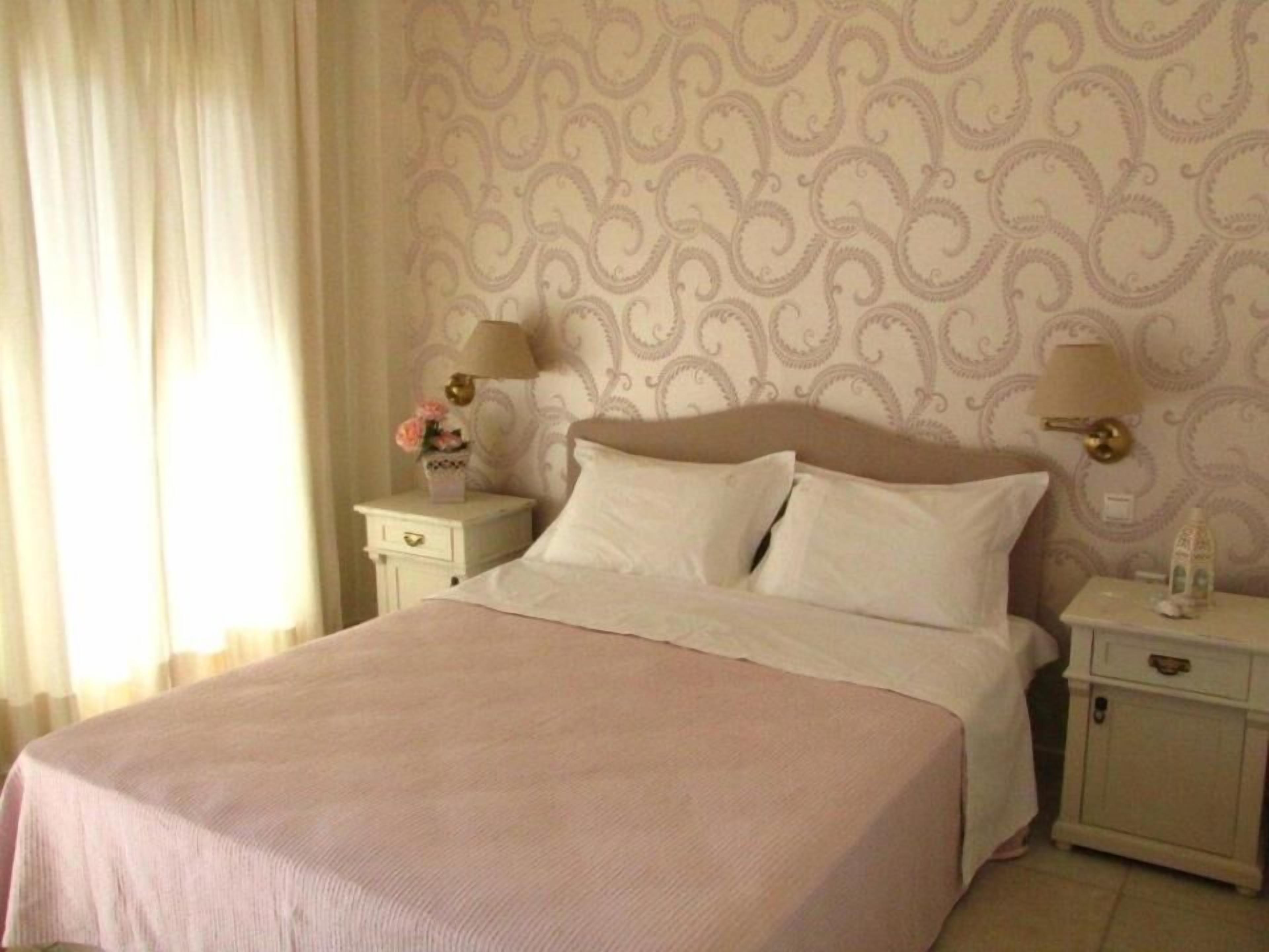 Uma cama bem arrumada com um edredom rosa, duas luminárias de cabeceira e uma mesinha de cabeceira com um vaso de flores.