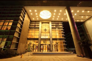 Entrada moderna de hotel com luminária circular sobre as portas, porta dupla no centro e um pilar vertical à direita.