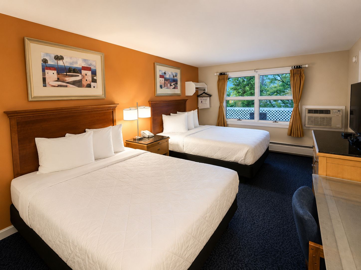 Quarto de hotel com duas camas, uma escrivaninha, televisão e janela com cortinas.