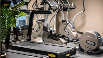 Fileira de bicicletas ergométricas em uma academia, com uma planta em primeiro plano.