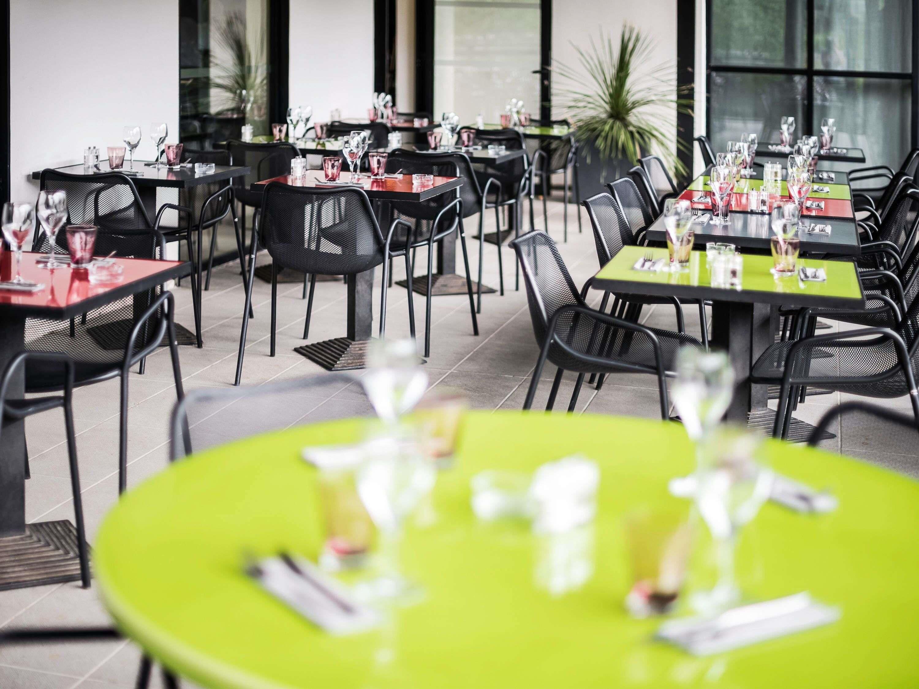 Restaurante com mesas preparadas para refeições, com uma combinação de toalhas de mesa vermelhas e verdes e cadeiras pretas.