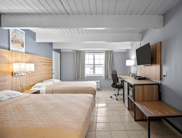 Quarto de hotel com duas camas, uma escrivaninha, uma cadeira, uma televisão e uma janela com cortinas.