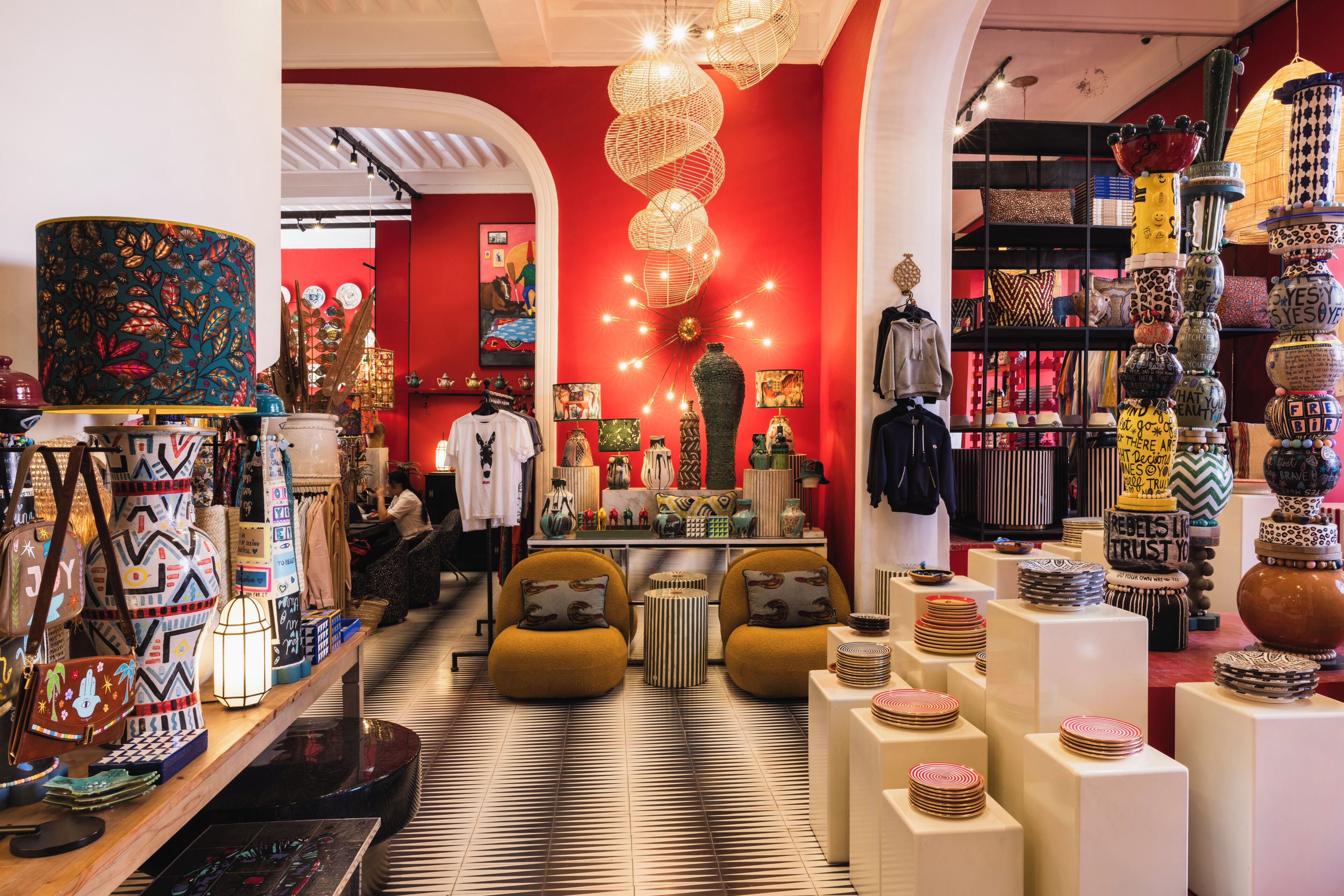 Interior de um hotel boutique com uma parede vermelha vibrante, tapetes estampados e diversos objetos decorativos em exposição.