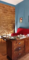 Quarto com parede de pedra, armário de madeira com gavetas, sofá vermelho e pequena mesa com bandeja de objetos.