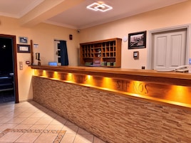 Balcão de recepção de hotel com bancada de madeira, área de recepção e uma porta ao fundo.