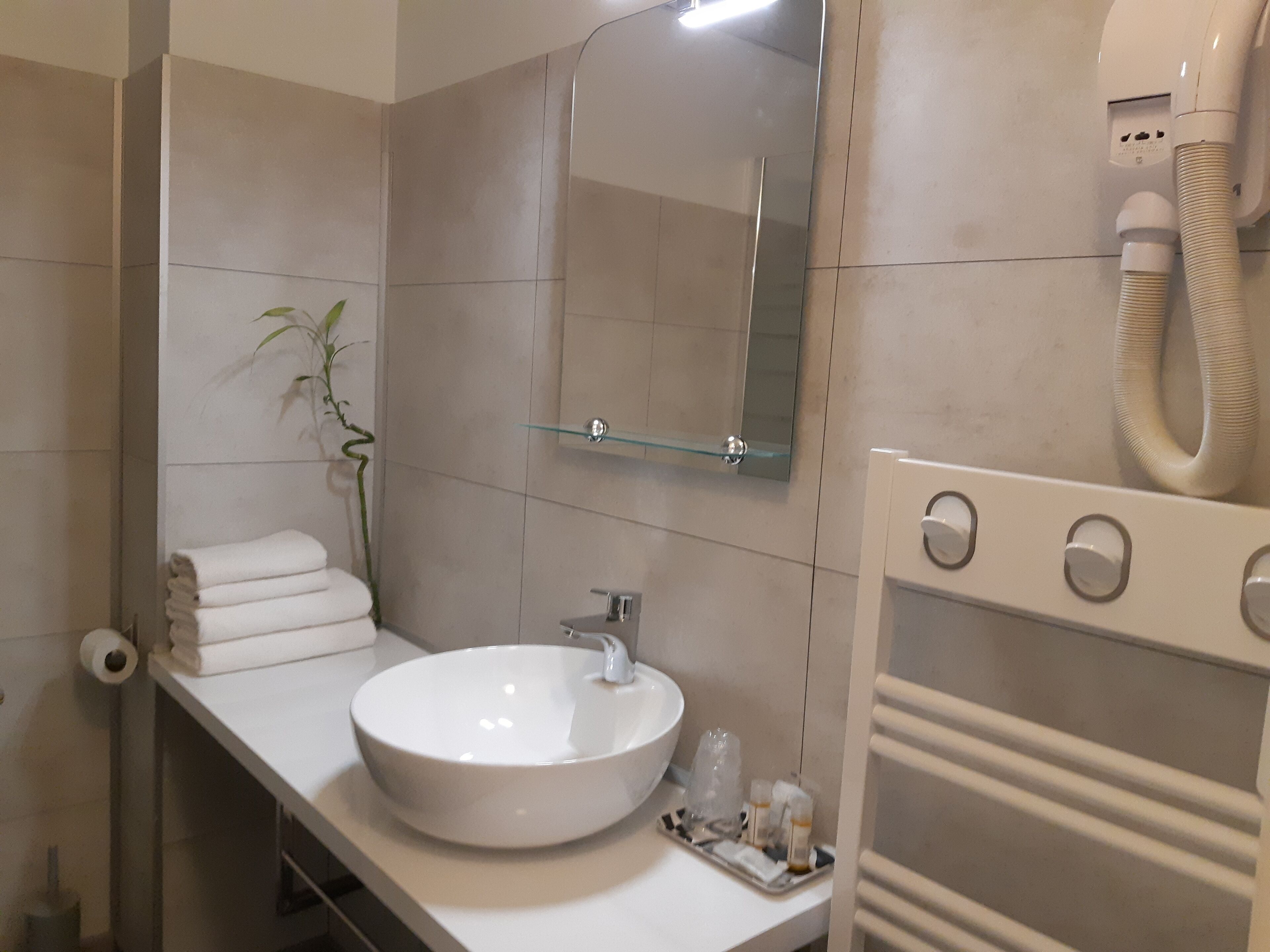 Uma casa de banho com uma pia branca, uma prateleira de vidro, um porta-toalhas e um espelho.