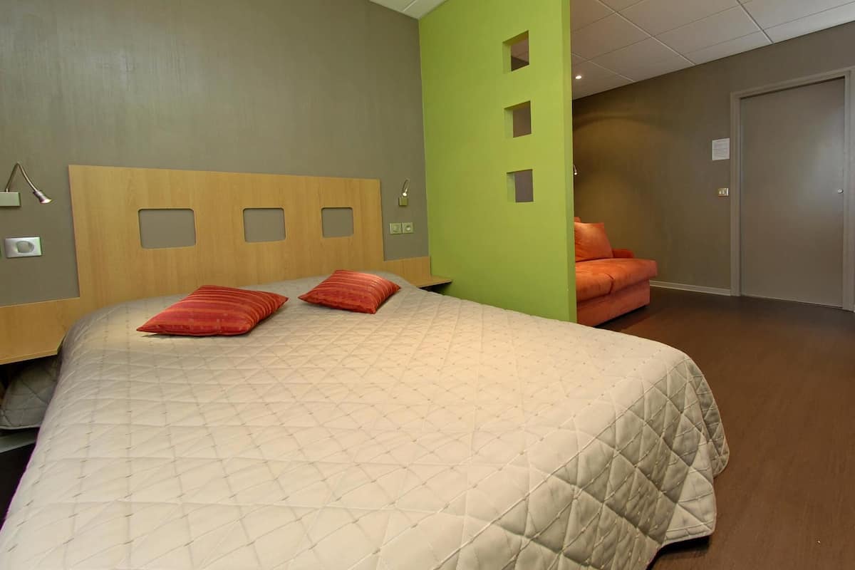 Quarto com cama, uma cadeira, uma porta e parede com painel verde.