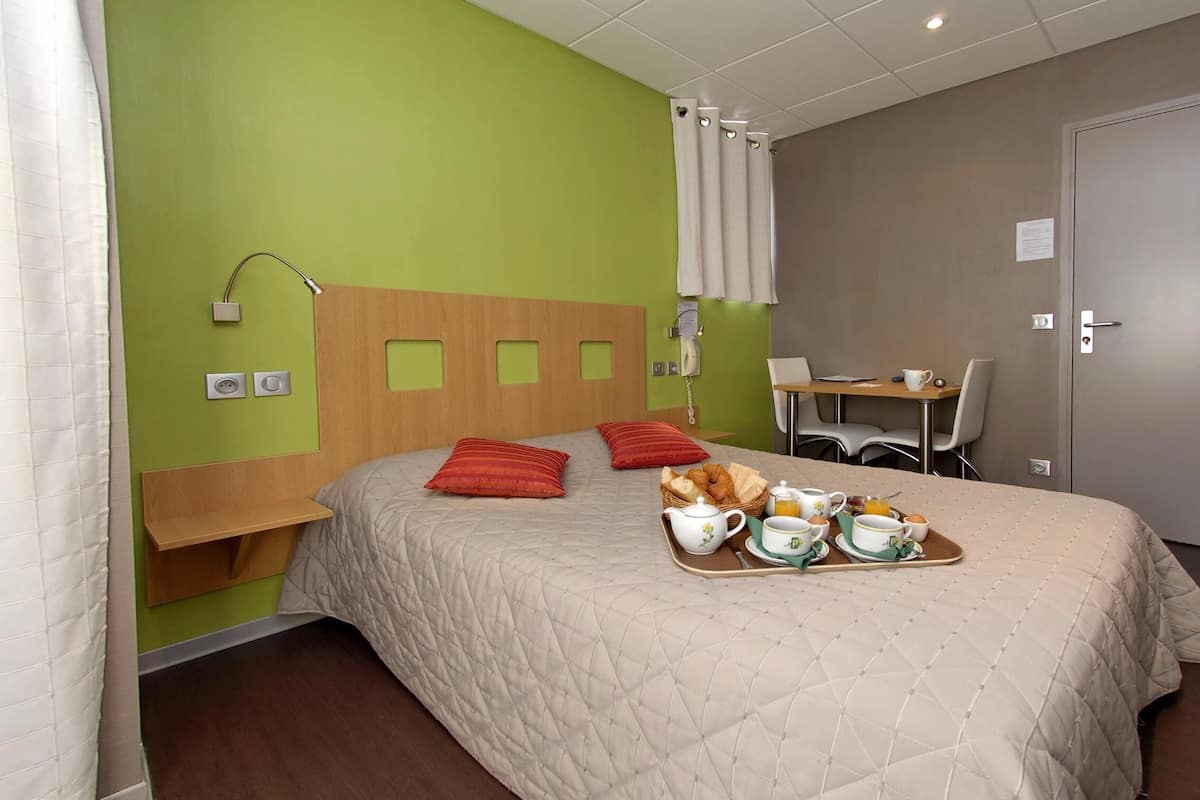 Quarto de hotel com cama, bandeja de café da manhã, mesa de cabeceira, escrivaninha, cadeira e telefone.