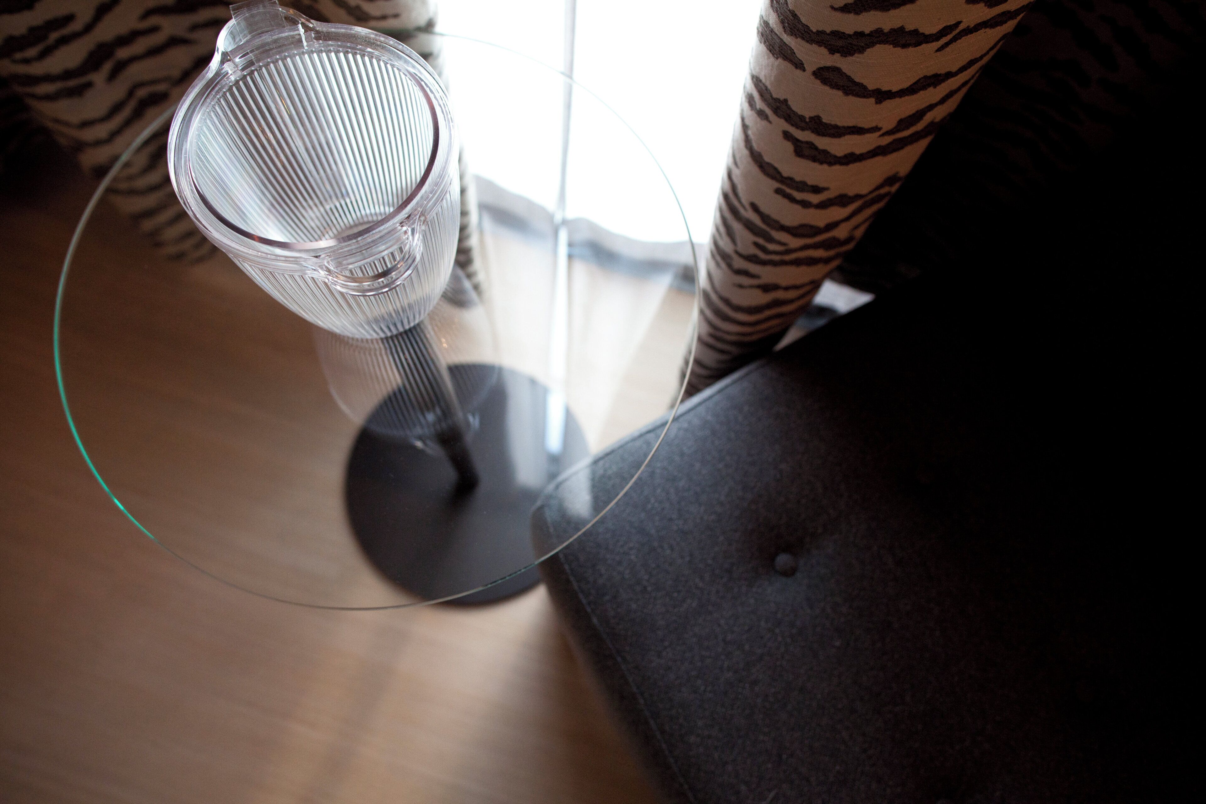 Mesa de vidro com peça central em tela metálica, base preta e tecido estampado em zebra na parede.