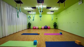 Um quarto amplo com piso de madeira, paredes verdes e redes de yoga aérea suspensas no teto. Há tapetes de exercícios e blocos de espuma dispostos no chão.
