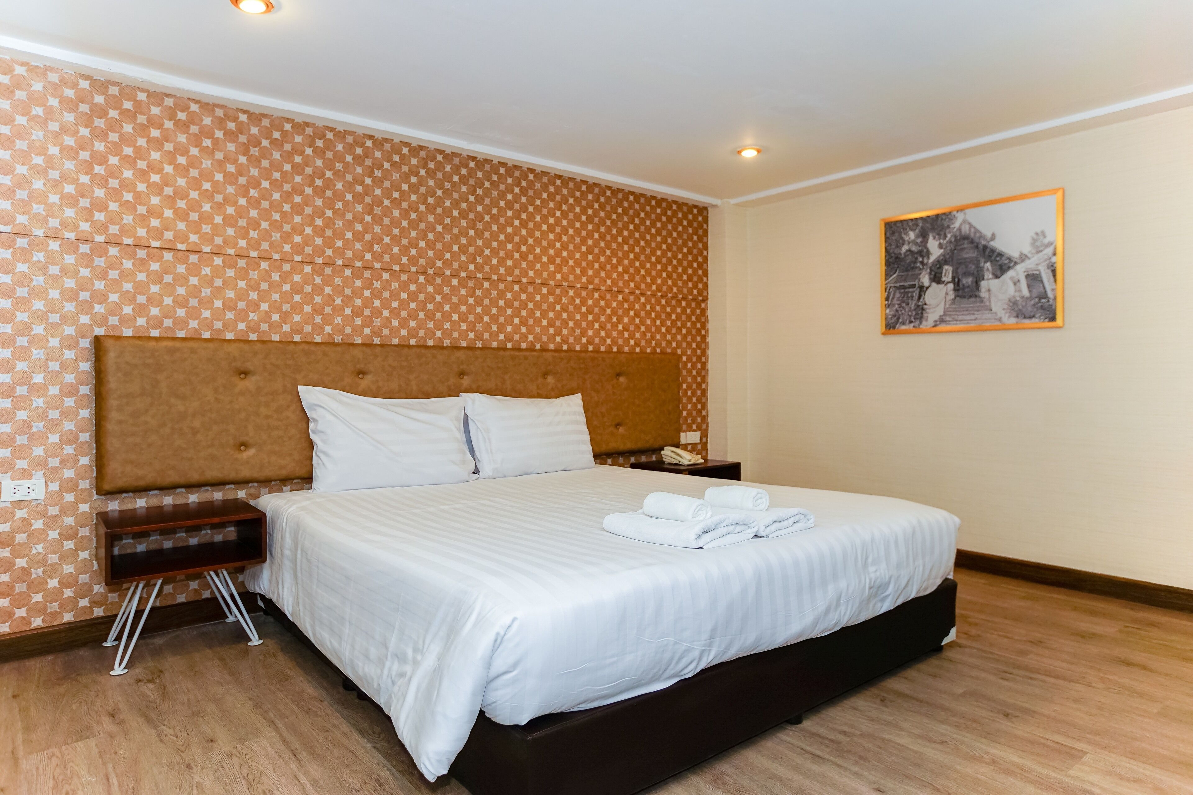 Cama bem arrumada com lençóis brancos, cabeceira de madeira e mesa de cabeceira com telefone.