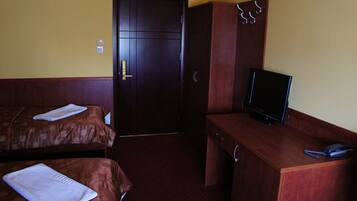 Quarto de hotel com duas camas, uma escrivaninha com televisão e um guarda-roupa.