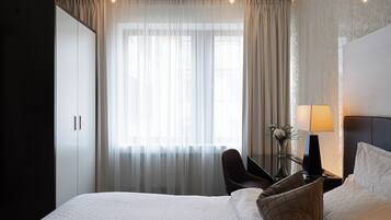 Quarto de hotel com cama, escrivaninha com luminária, cadeira e guarda-roupa.