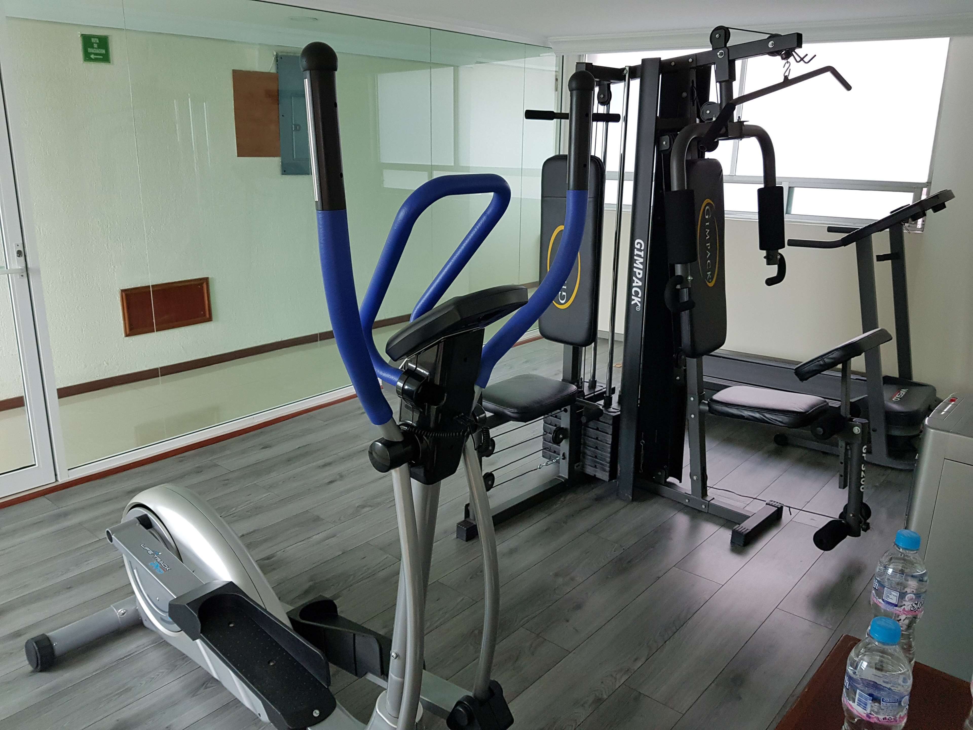 Academia com equipamentos de ginástica, incluindo esteira, elíptico e aparelhos de musculação.