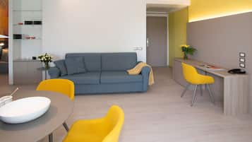 Uma sala de estar moderna com um sofá cinzento, cadeiras amarelas, uma mesa de jantar e uma área de cozinha com prateleiras e um vaso de flores.