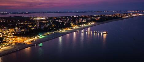 Paisagem costeira urbana ao anoitecer, com uma orla bem iluminada, uma ponte e mar calmo.