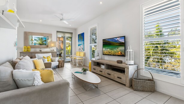 Uma sala de estar moderna com sofá, mesa de centro, TV e janelas amplas com persianas.