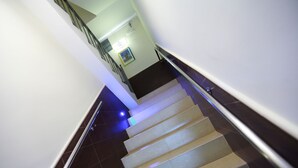 Uma escadaria com corrimão, que leva a um patamar com luminária e quadro emoldurado.